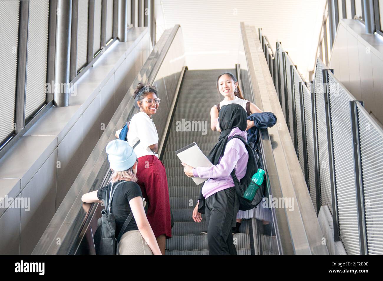 Group of happy young female students going up the escalator. Back to ...