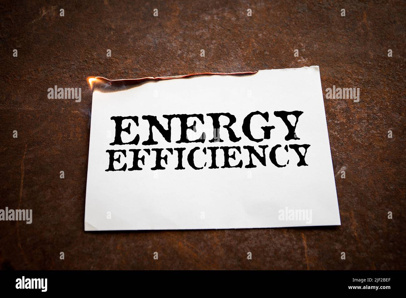 ENERGY EFFICIENCY. Burning paper with text on a rusty metal background ...