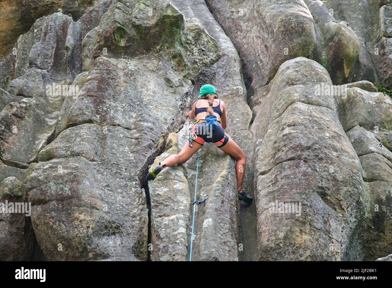 Determined girl climber clambering up steep wall of rocky mountain ...