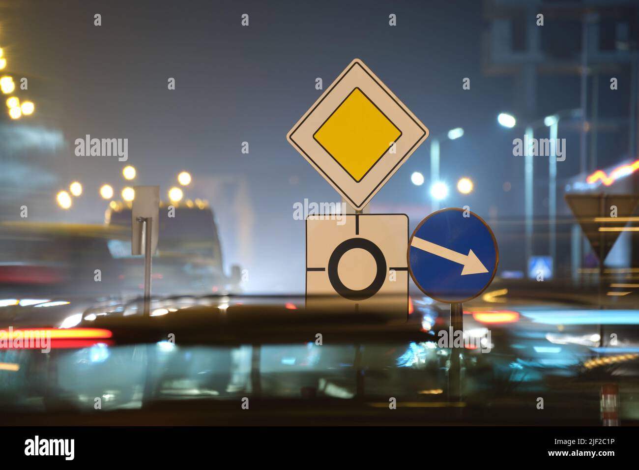 Roundabout road signs with blurred cars on city street traffic at night ...