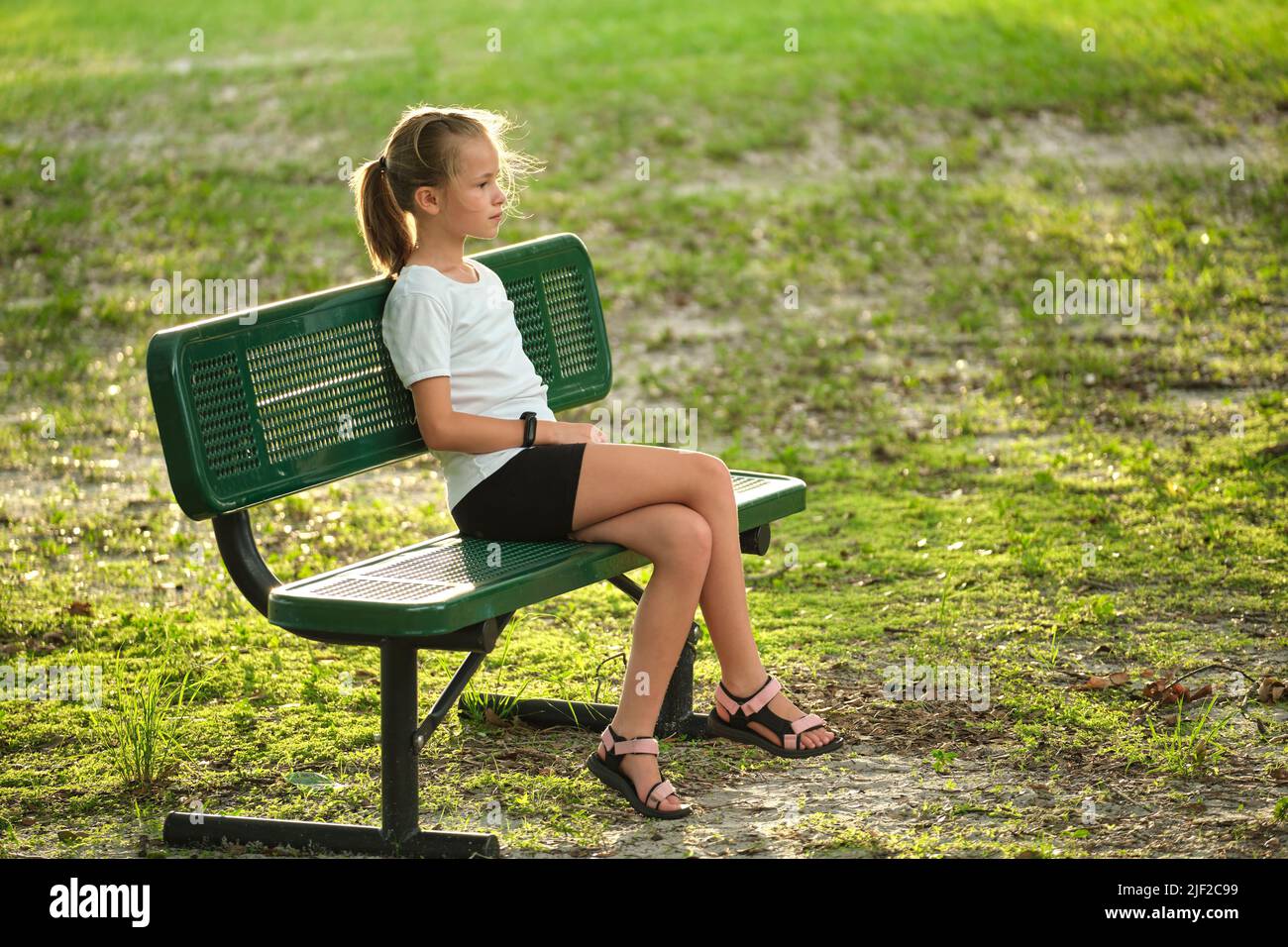 Young pretty child girl with dreamy smile resting on bench in backyard ...