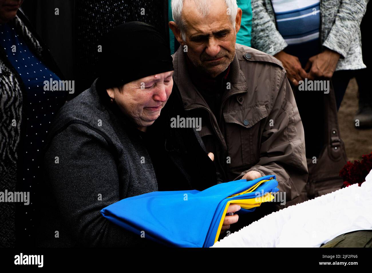 Mother is crying, while she holds the Ukrainian flag in her hands. Family, relatives, and ...
