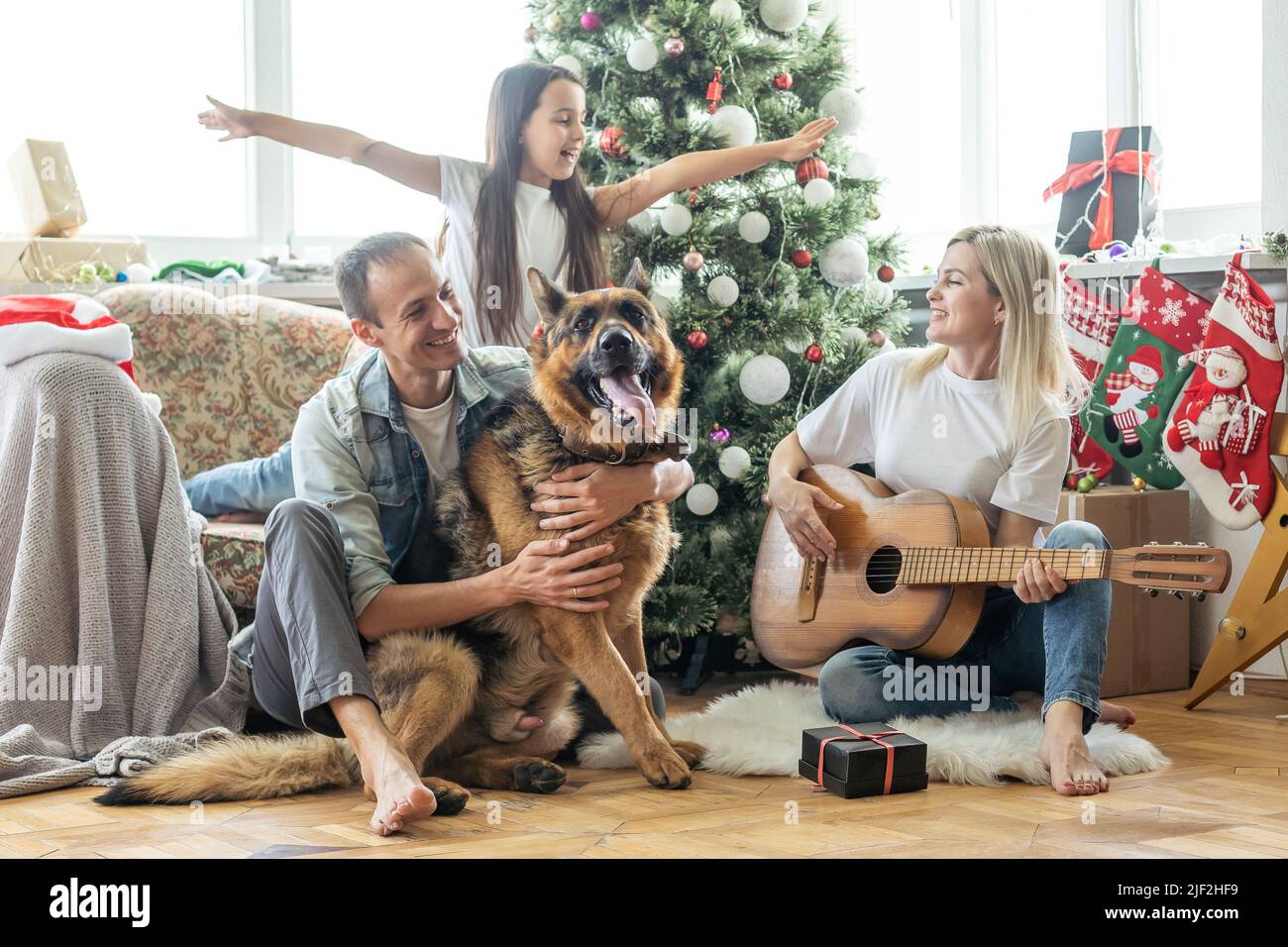 smiling family and daughter with dog sitting near christmas tree with ...