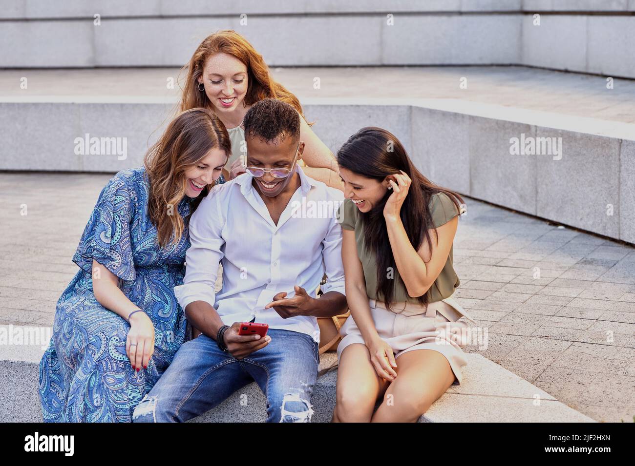 Group of friends using a mobile phone together while sitting outdoors ...