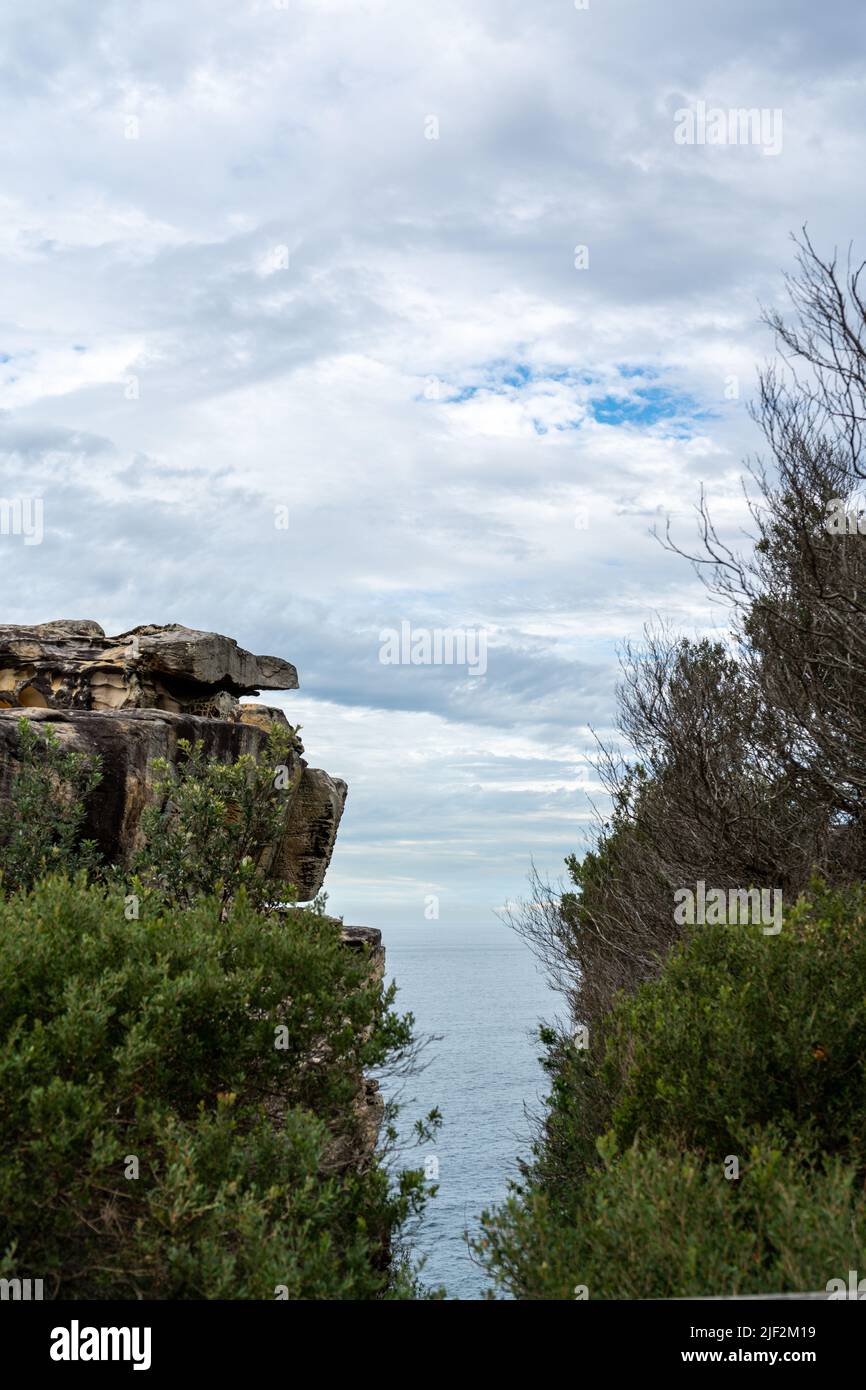 A vertical of a rocky cliff covered with greenery against a blue sea ...