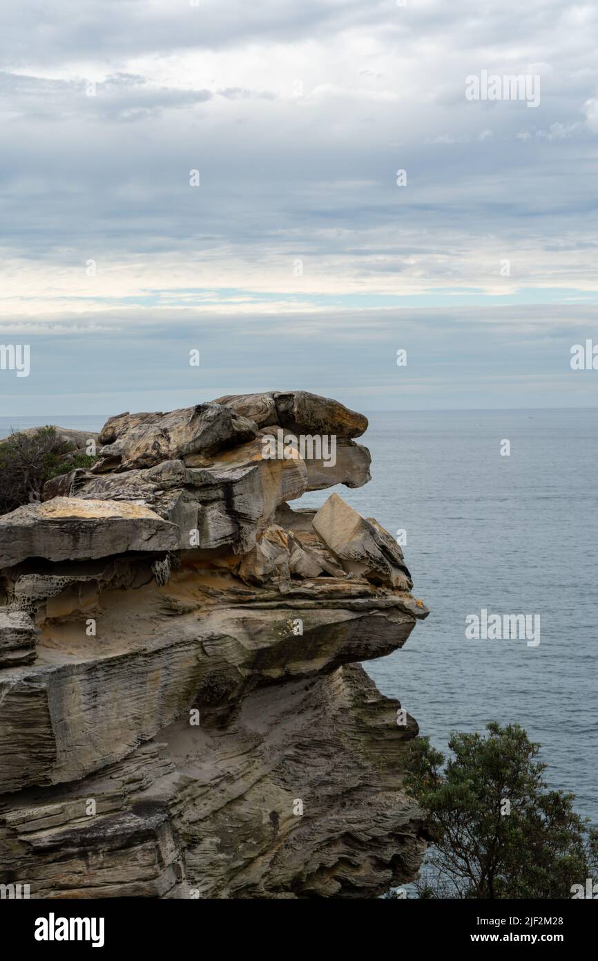 A vertical of a rocky cliff covered with greenery against a blue sea ...