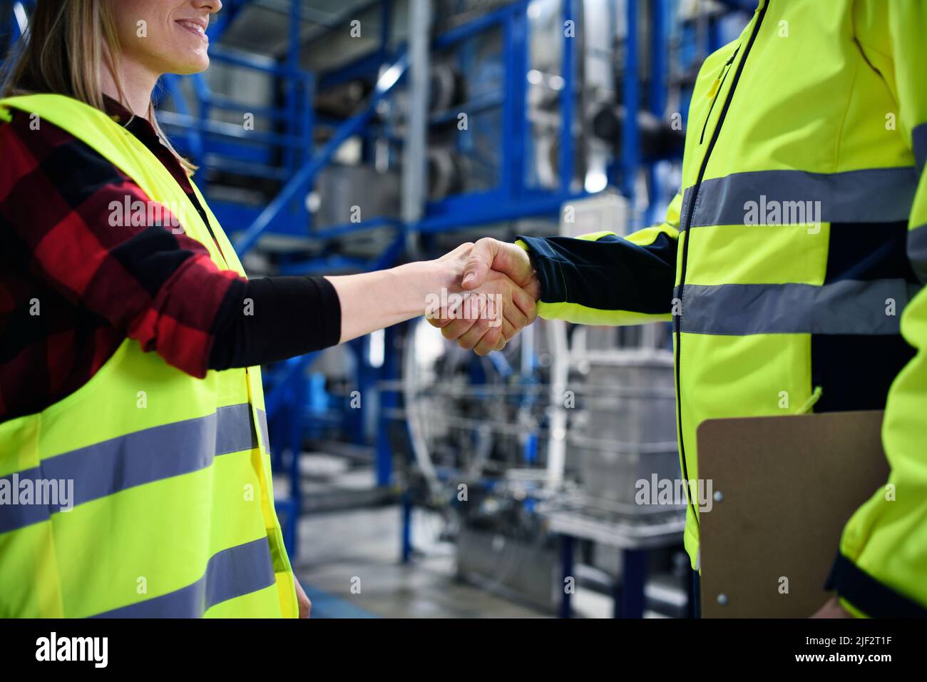 Engineer and industrial worker in uniform shaking hands in large metal ...