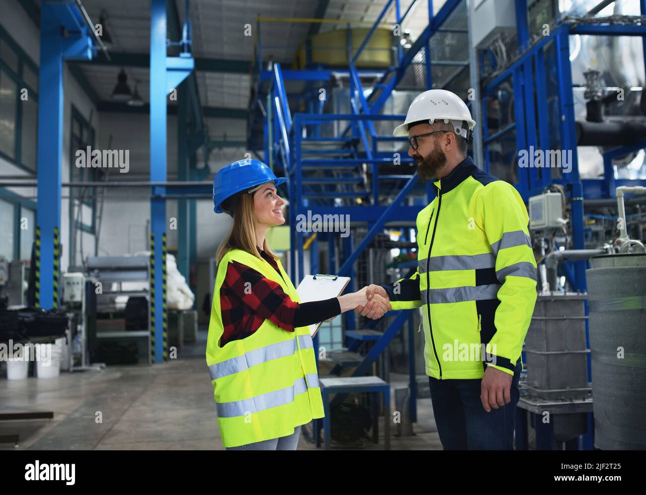 Engineer and industrial worker in uniform shaking hands in large metal ...