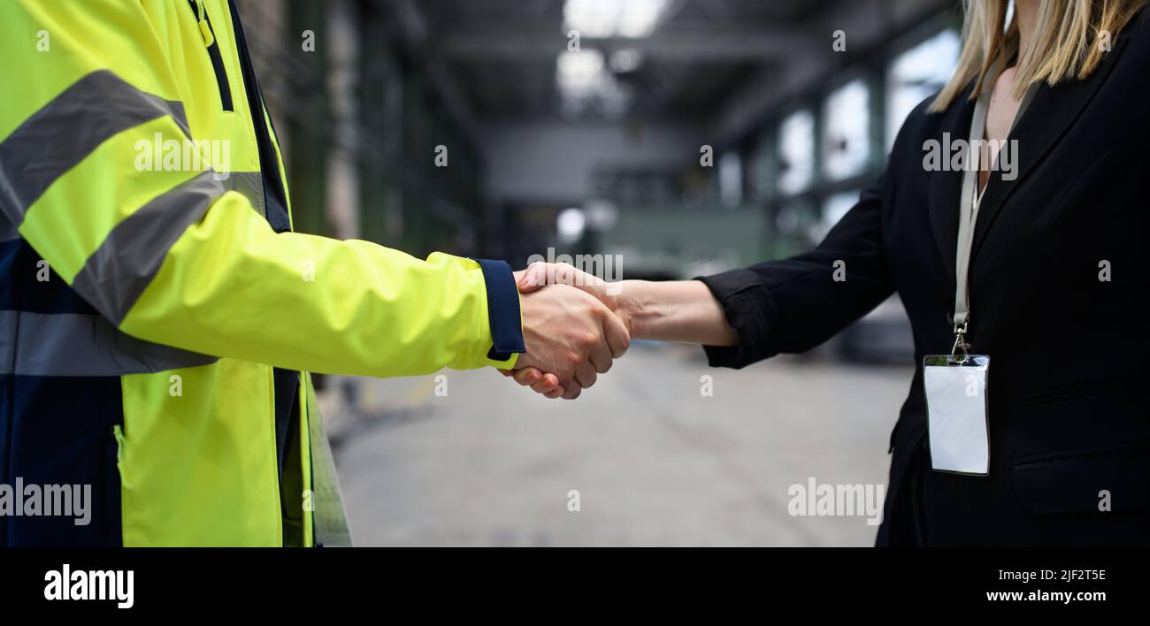 Engineer and industrial worker in uniform shaking hands in large metal ...