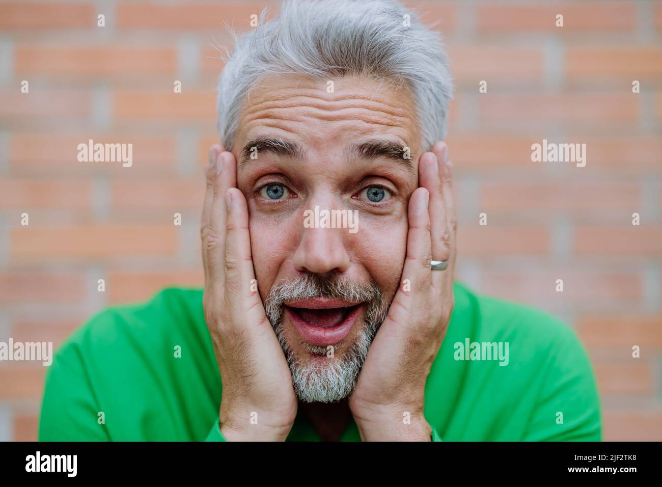 Mature man with shocked, amazed expression touching his face on street ...