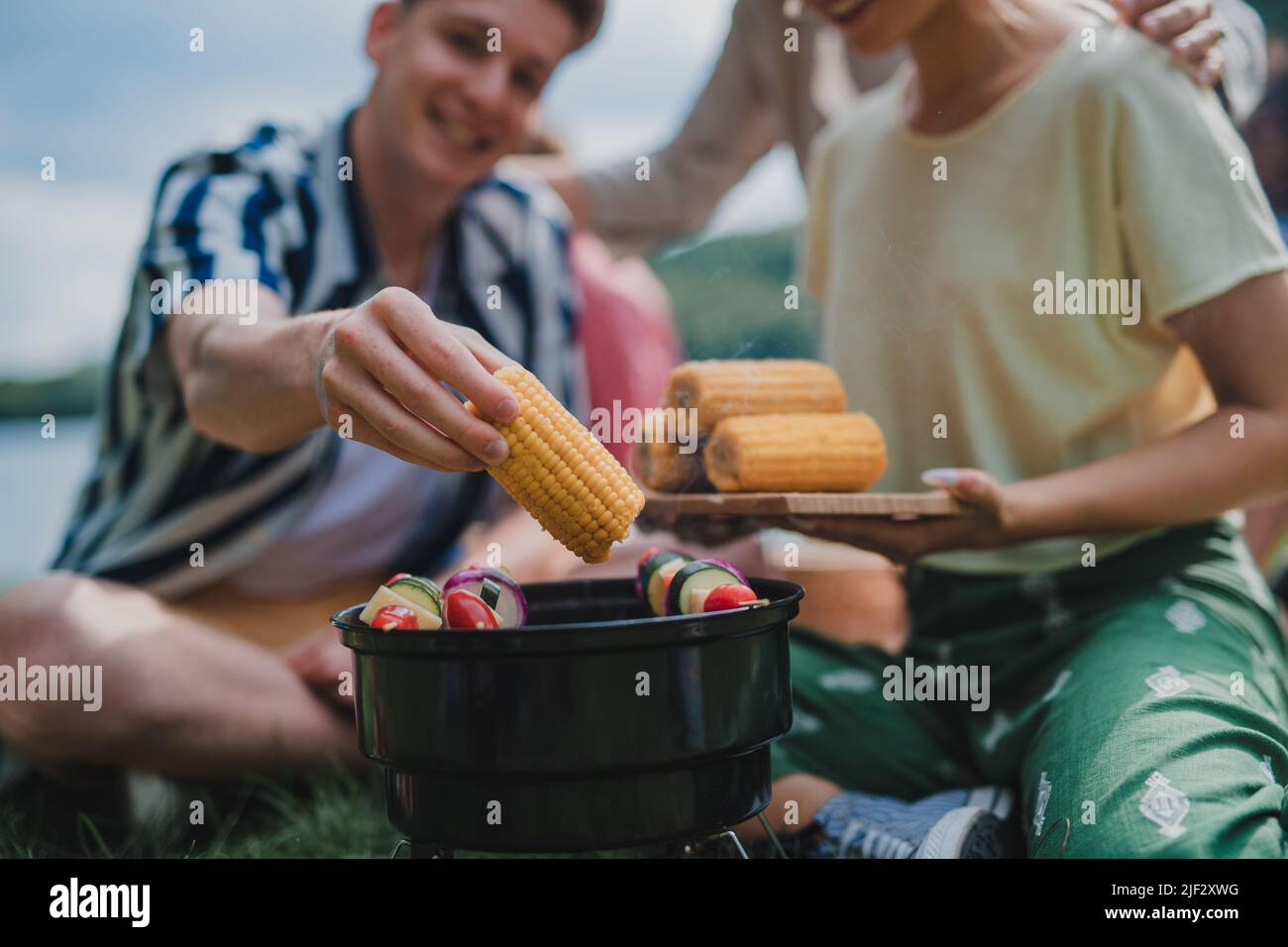 Close-up of young friends putting corn on grill and having barbecue ...