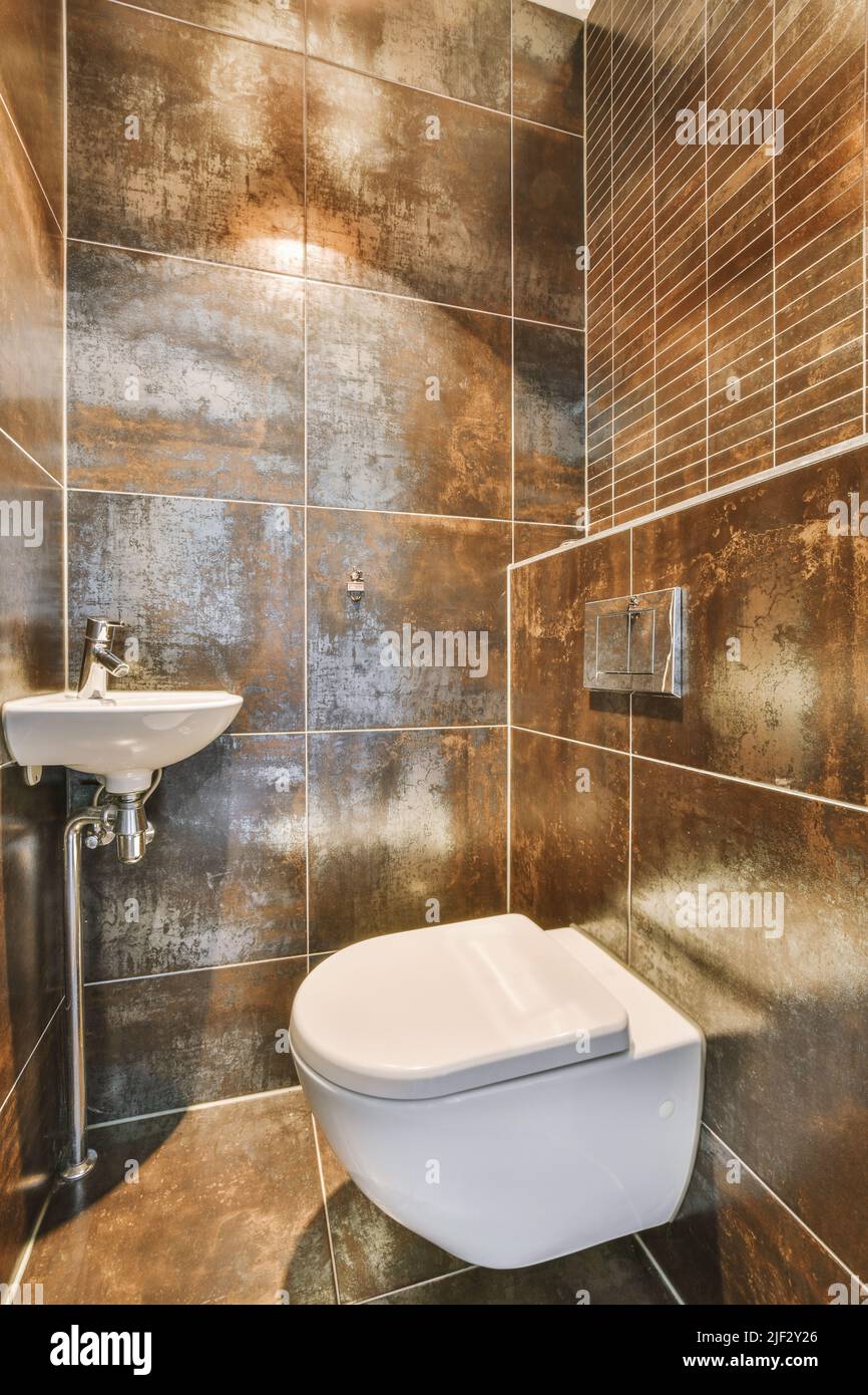 Wall hung toilet and small sink in corner in lavatory room with beige ...