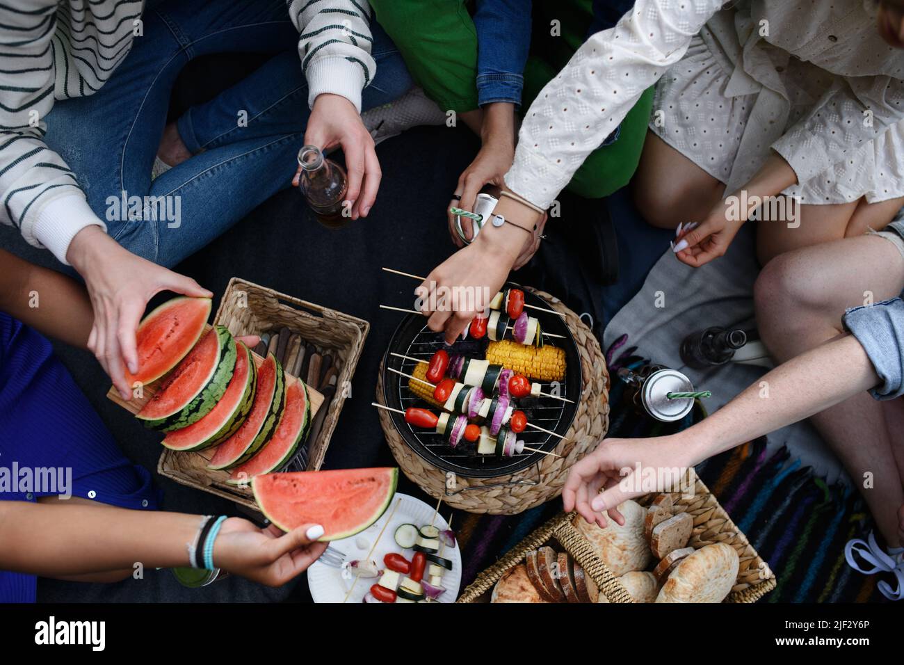 A close-up of young friends putting corn and skewers on grill and ...
