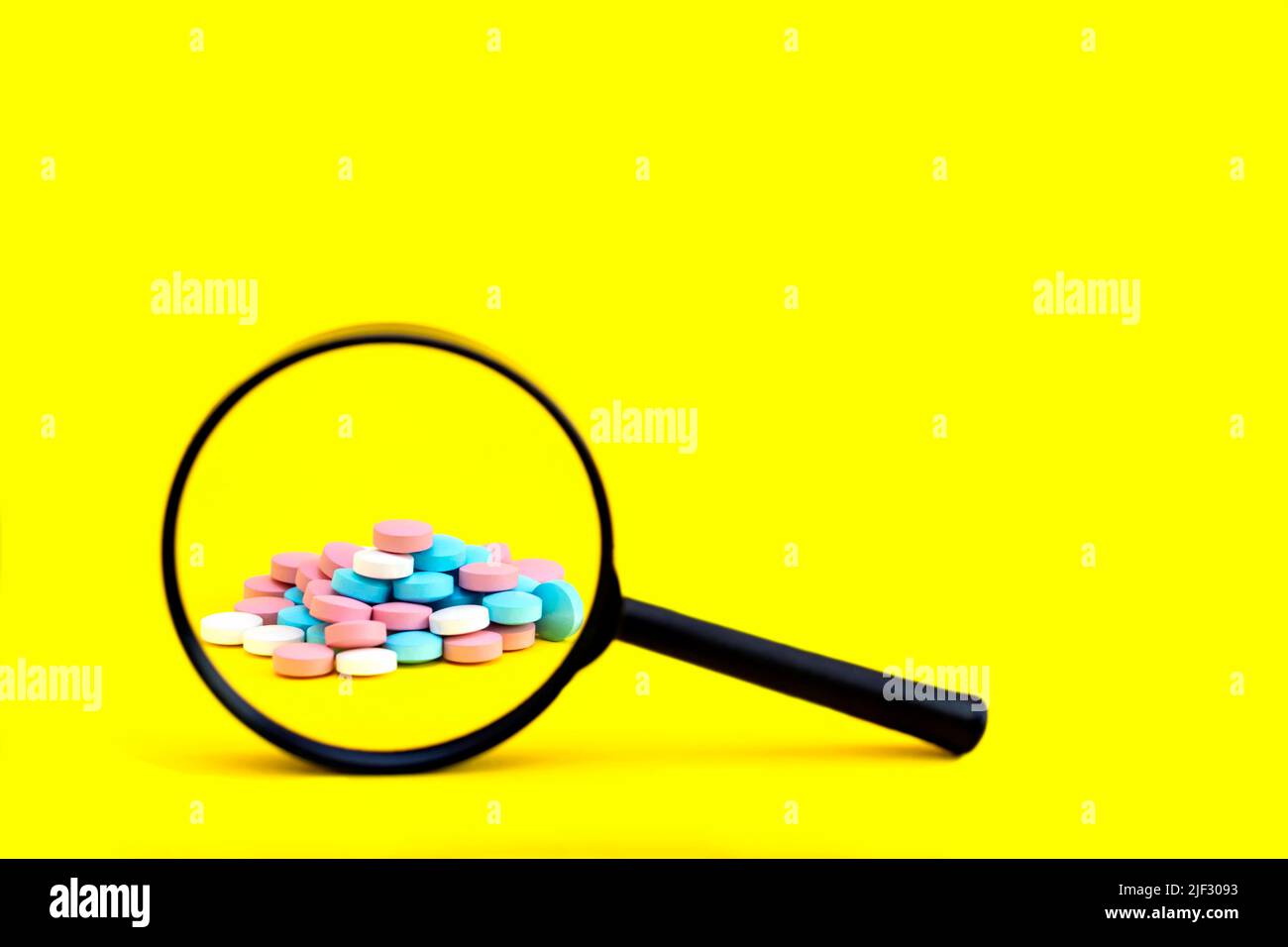 A look through a magnifying glass at a pile of pills on a yellow ...