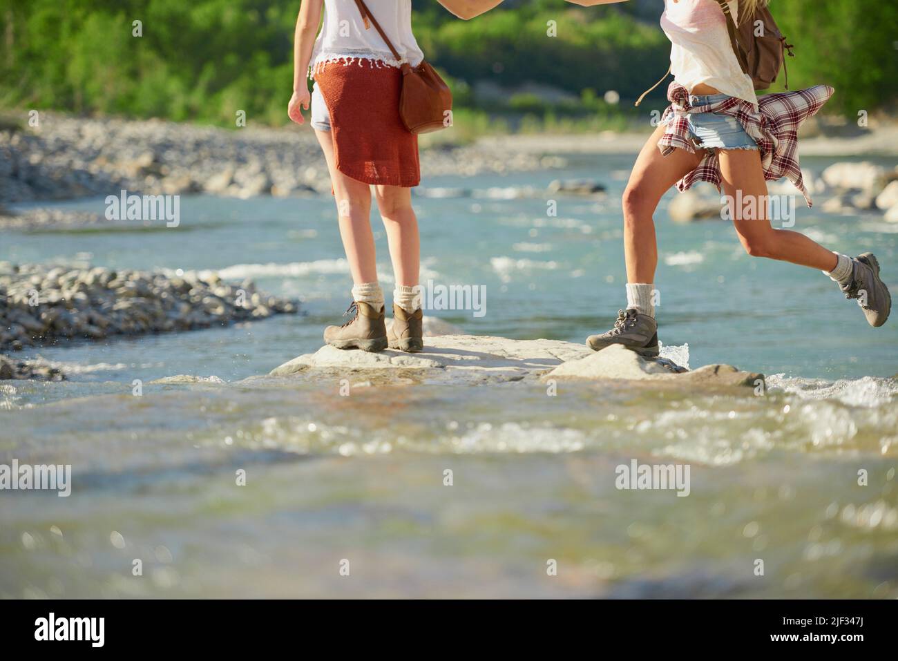 Two friends walking over rocks crossing a river during a hiking trip ...