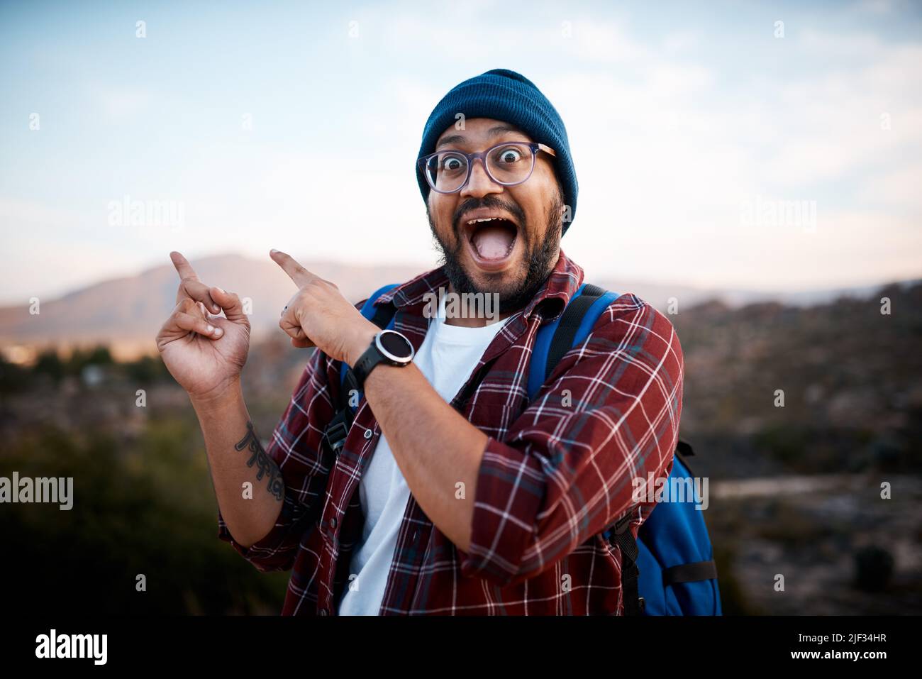 An excited backpacker points to the mountain view behind him on hiking ...
