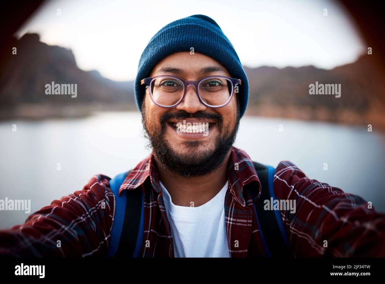 A happy hiker takes a selfie at the summit with a lake and mountains ...