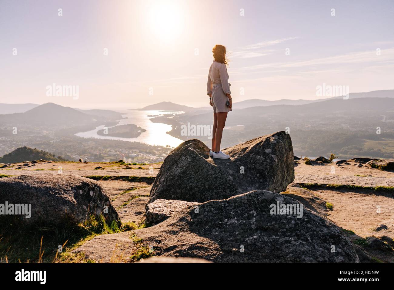 Young woman contemplating the landscape from the top of a rock, with a ...