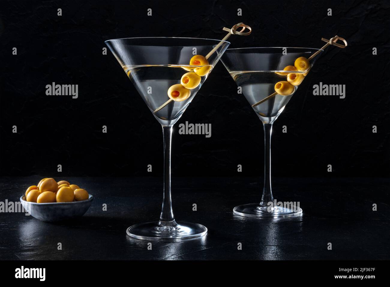 Martini, two glasses with spicy olives, on a dark background. Alcoholic ...