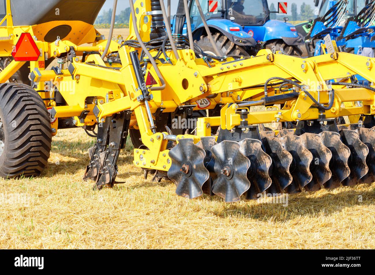 A yellow disc harrow clings to a wheeled agricultural tractor for ...