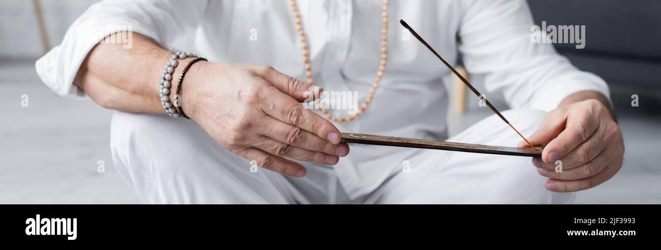 cropped view of guru man in beaded bracelets holding aroma stick ...