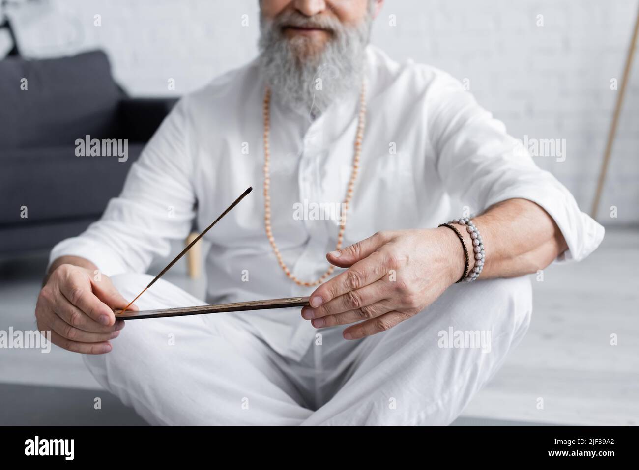 partial view of guru man in white clothes and beaded bracelets holding ...