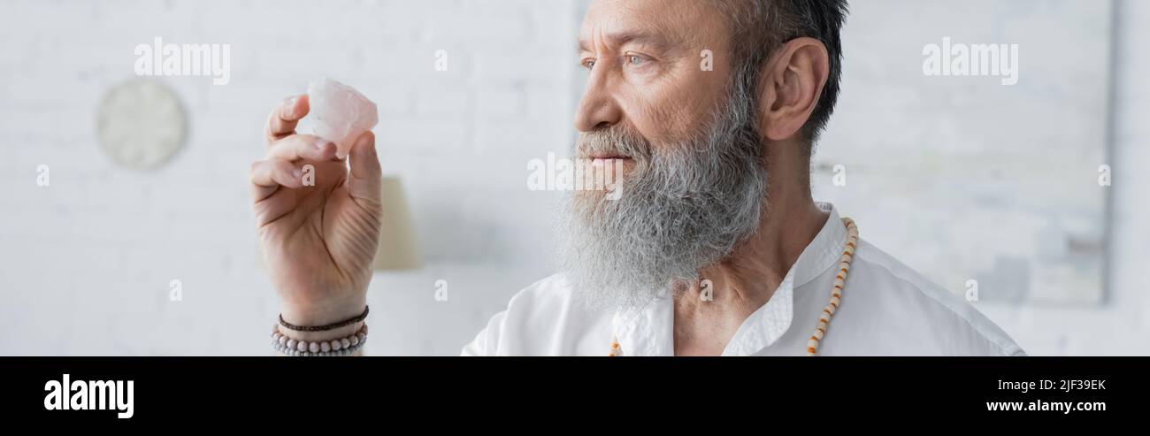 bearded guru man looking at selenite crystal while meditating at home ...