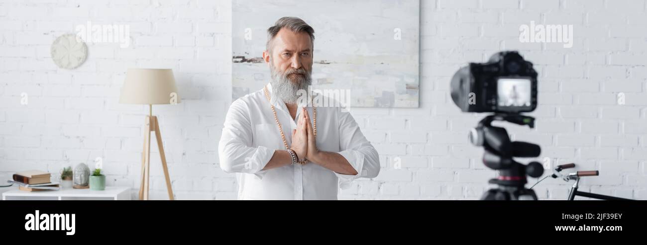 bearded guru man meditating with praying hands near digital camera ...