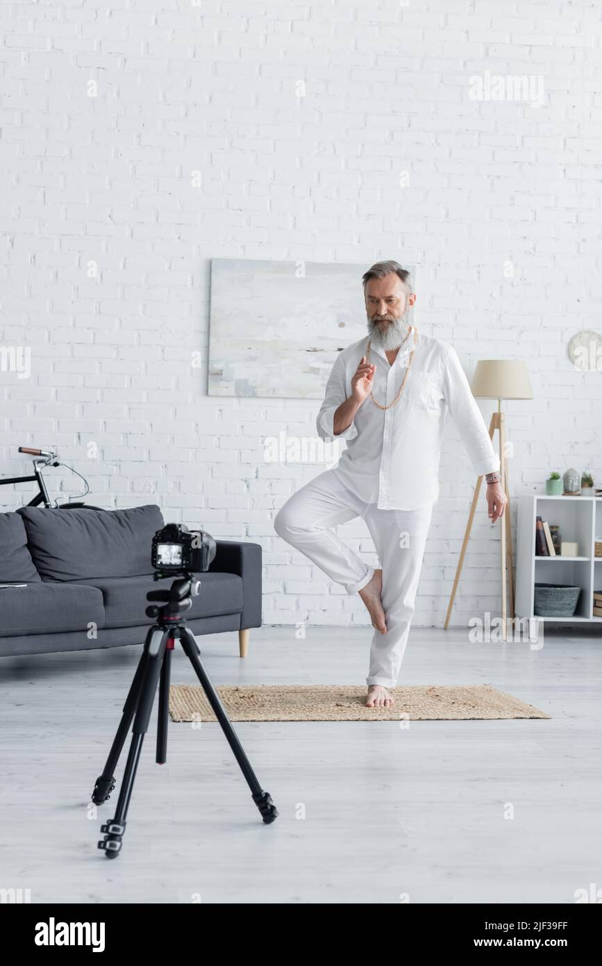 senior yoga coach showing tree pose and prana mudra gesture in front of ...