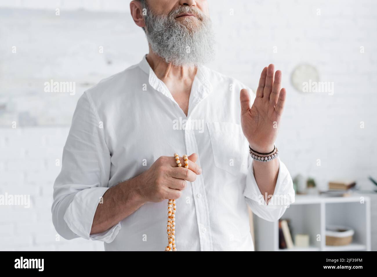 partial view of master guru holding rosary and showing blessing gesture ...