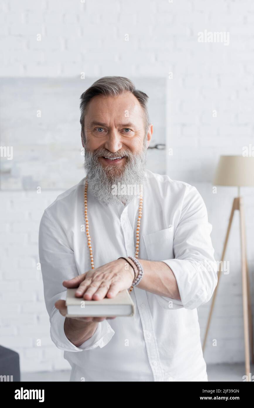 happy spiritual coach looking at camera while holding book Stock Photo ...
