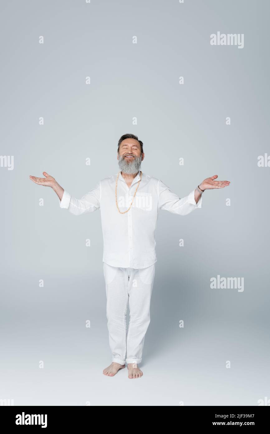 full length of smiling yoga guru meditating in tree pose with open arms ...