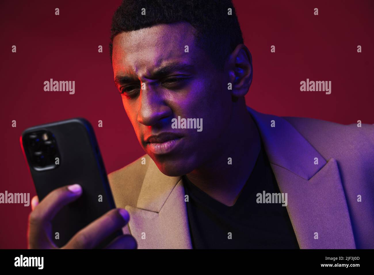 Young black man dressed in jacket frowning while using cellphone ...