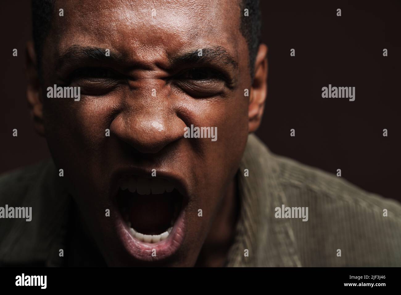 Young black man frowning and screaming at camera isolated over brown ...