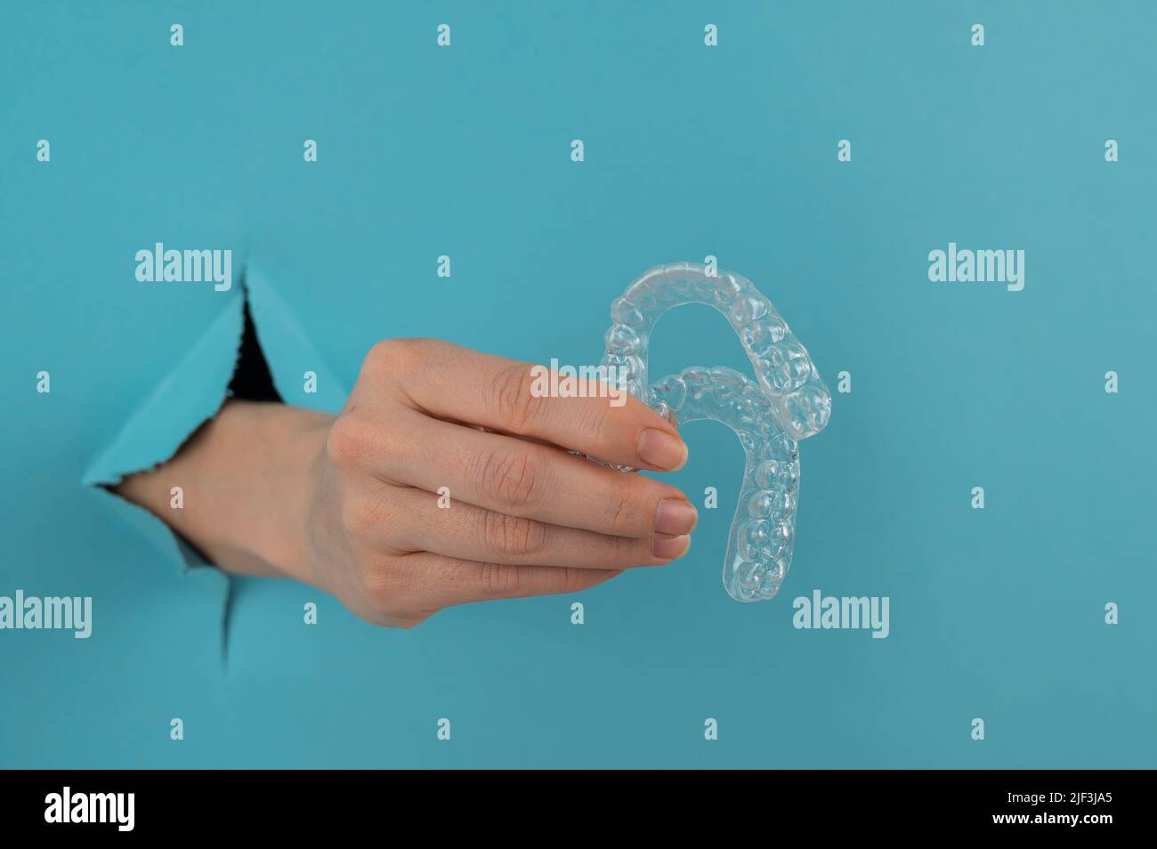 A female hand sticking out of a hole from a blue background holds ...