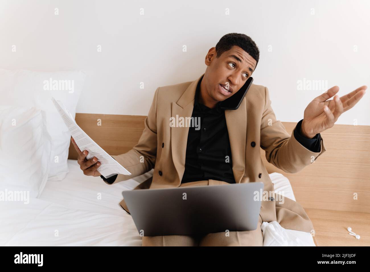 Black man talking on cellphone while working with laptop and documents ...