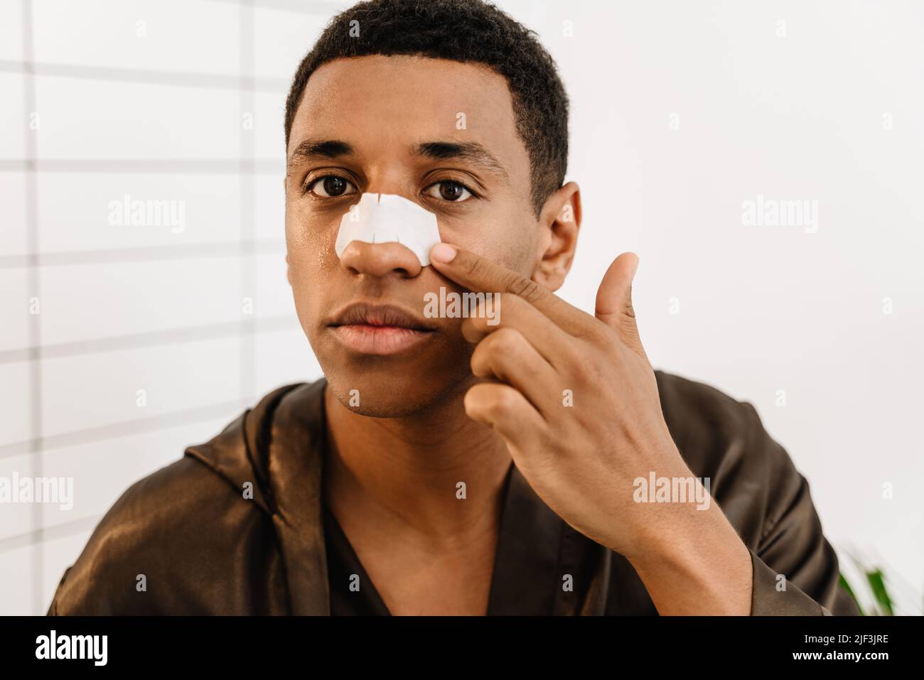 Black man using nose patch against blackheads in bathroom at hotel ...
