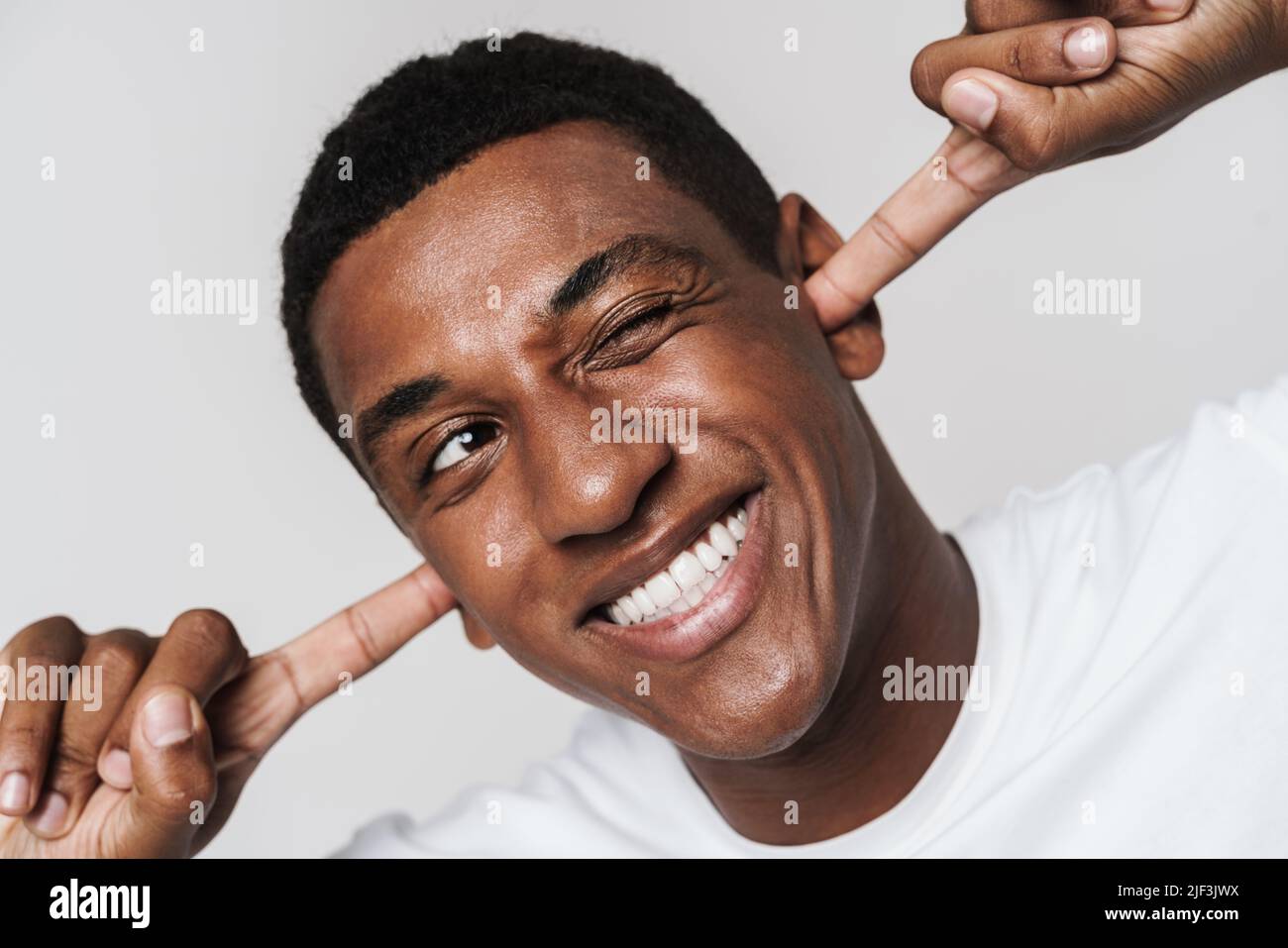Young black man smiling and winking while plugging his ears isolated ...