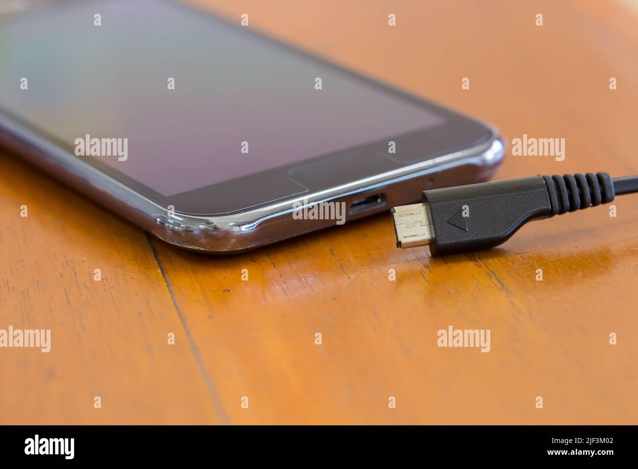 Close up of smart phone charging with USB cable on wooden texture ...
