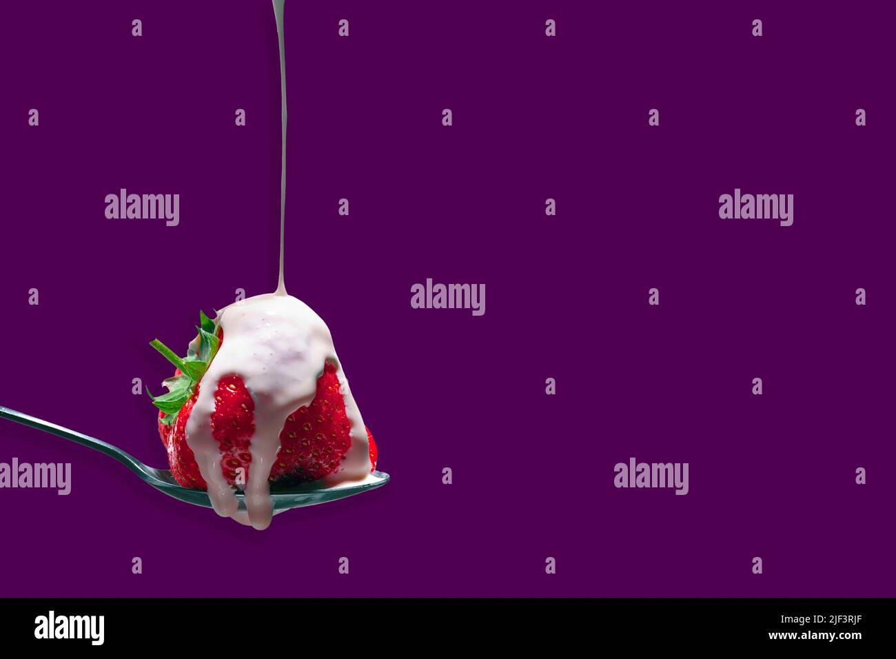 Cream being poured over a single ripe strawberry on a spoon against a ...