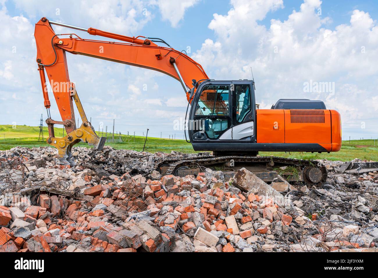 Orange crusher excavator stands sideways on ruins of brick building ...