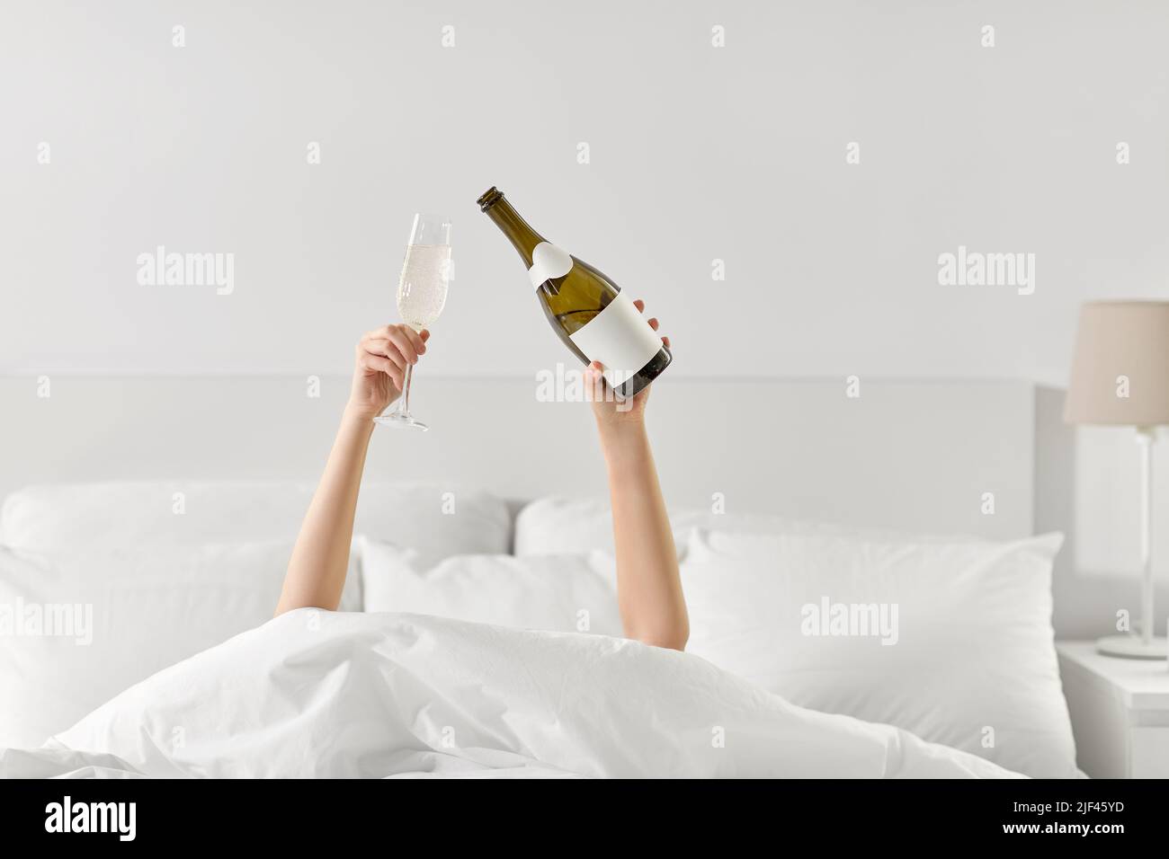 hands of woman lying in bed with champagne Stock Photo - Alamy