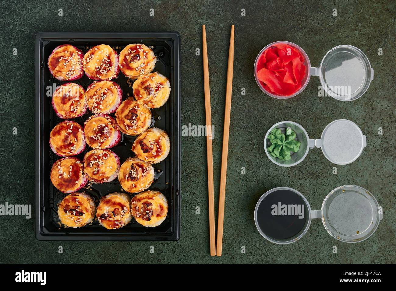 Baked salmon and eel rolls in a plastic takeout tray, jars with ginger ...