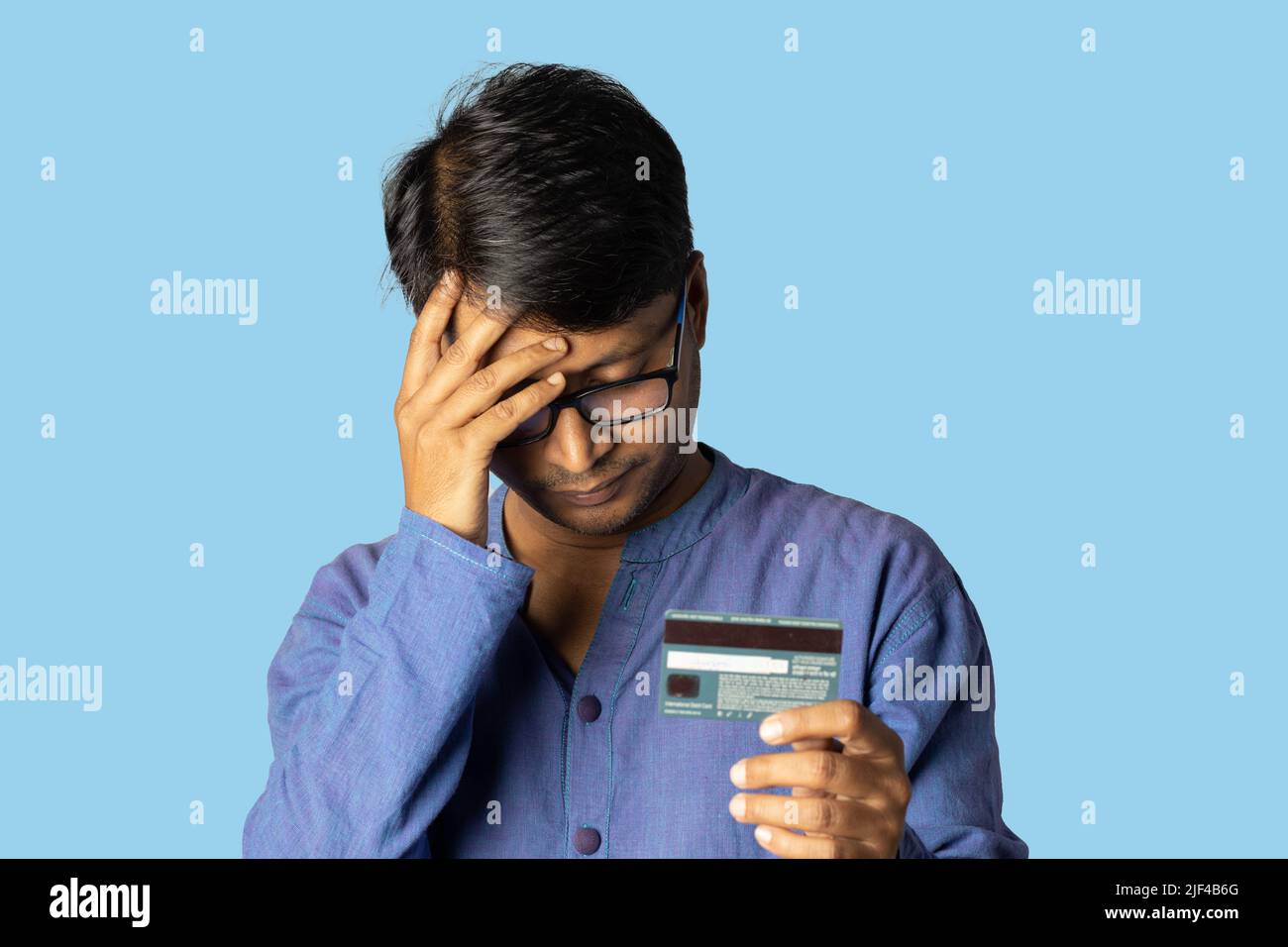 A middle aged Indian male wearing spectacles with worried face holding ...
