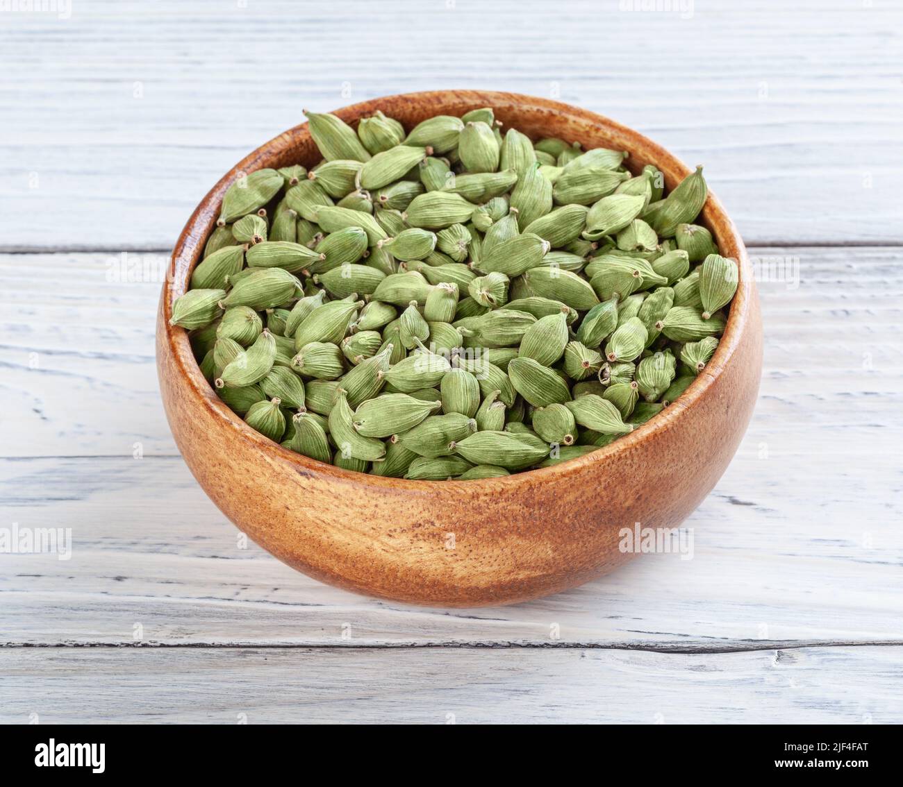 Cardamom pod in wooden bowl on white wooden background Stock Photo - Alamy
