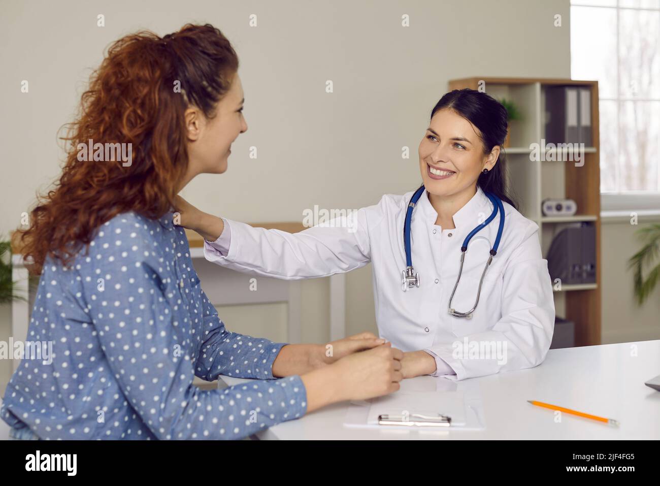 Doctor touches patient's shoulder telling her good news during ...