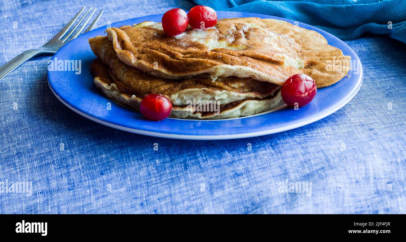Straight on view of a stack of Banana Pancakes topped with cherries and ...