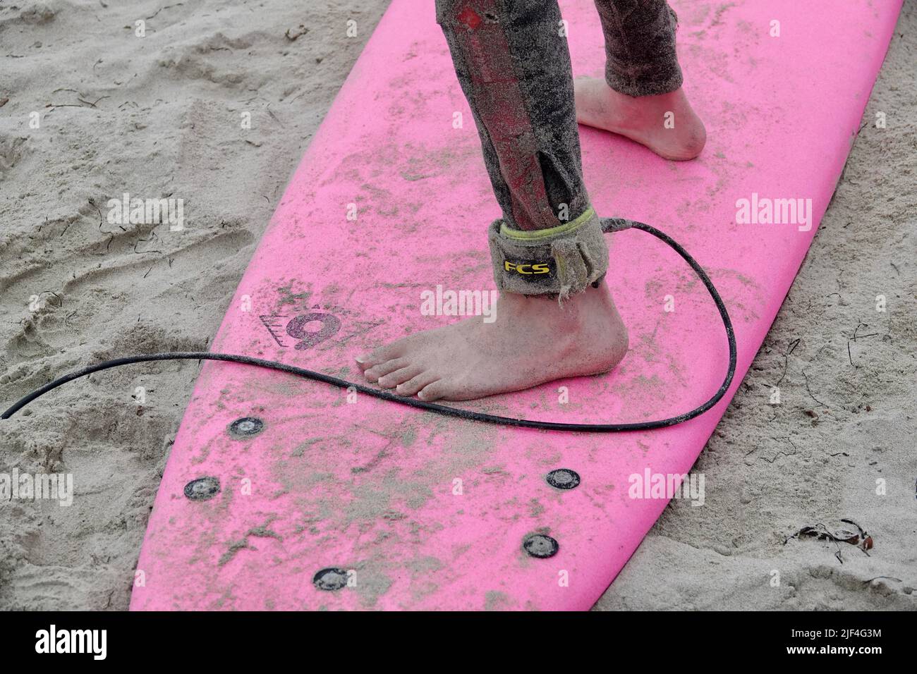A close up of feet standing on a surfboard lying on the sand Stock ...