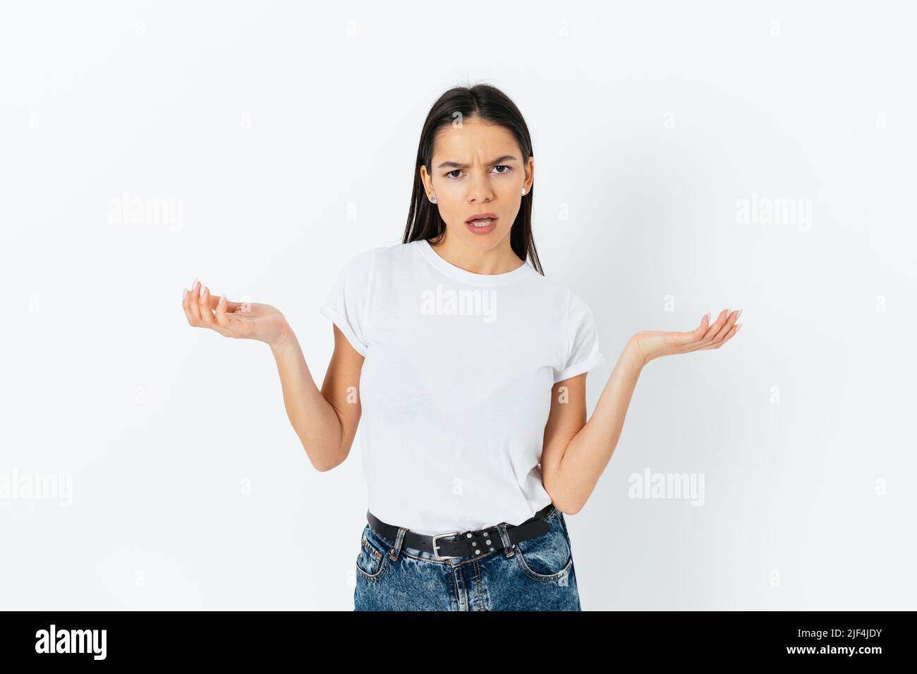 Portrait of irritated young brunette woman standing on white studio ...