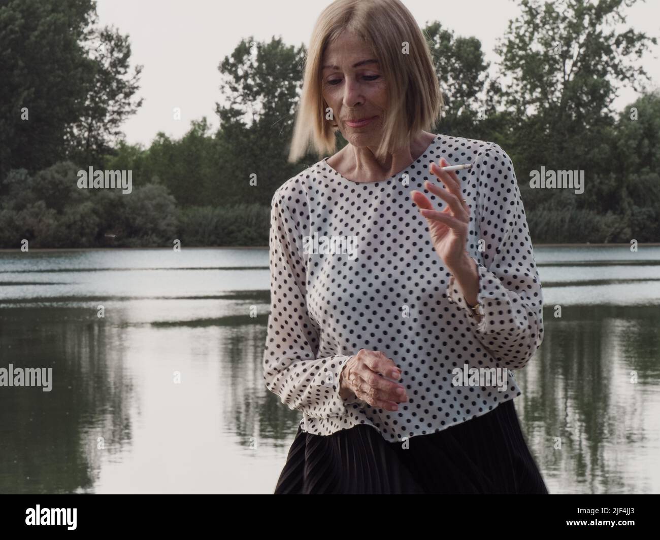 female pensioner having fun and smoking a cigarette in a park - aging ...